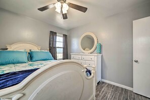 Quarto com cama, cômoda, espelho e ventoinha no teto.