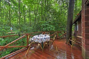 Um deck de madeira com mesa e cadeiras, cercado por uma floresta densa.