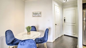 Uma área de refeições com mesa de mármore e cadeiras azuis, uma planta em vaso e uma porta branca ao fundo.