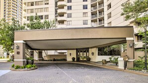 Entrada de hotel com galeria coberta, vasos de plantas e uma placa.