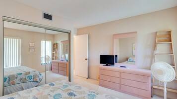 Quarto com cama, cômoda, espelho, televisão e ventilador.
