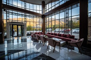 Um hall amplo com design moderno, com área de estar com sofás e poltronas, janelas amplas com vista para as montanhas e piso refletivo.