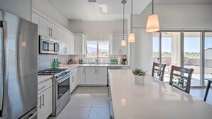 Uma cozinha moderna com eletrodomésticos de aço inoxidável, armários brancos e iluminação pendente.