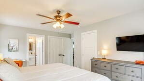 Quarto com cama, penteadeira, ventilador de teto e televisão na parede.
