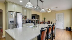 Uma cozinha moderna com ilha central, eletrodomésticos de aço inoxidável, iluminação pendente e uma área de refeições com cadeiras.