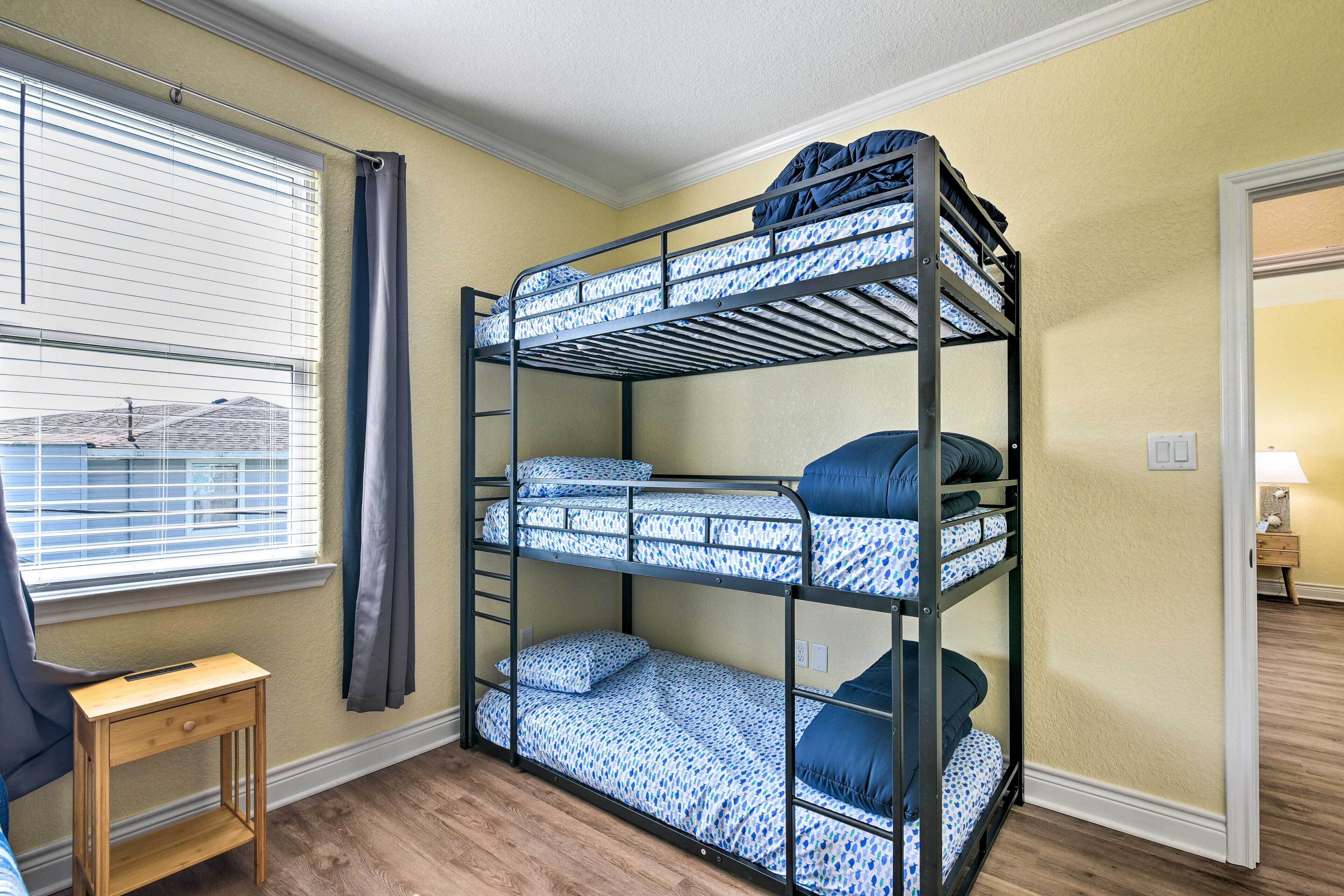 Quarto com beliche, janela, uma pequena mesa de madeira e porta que dá para outro espaço.