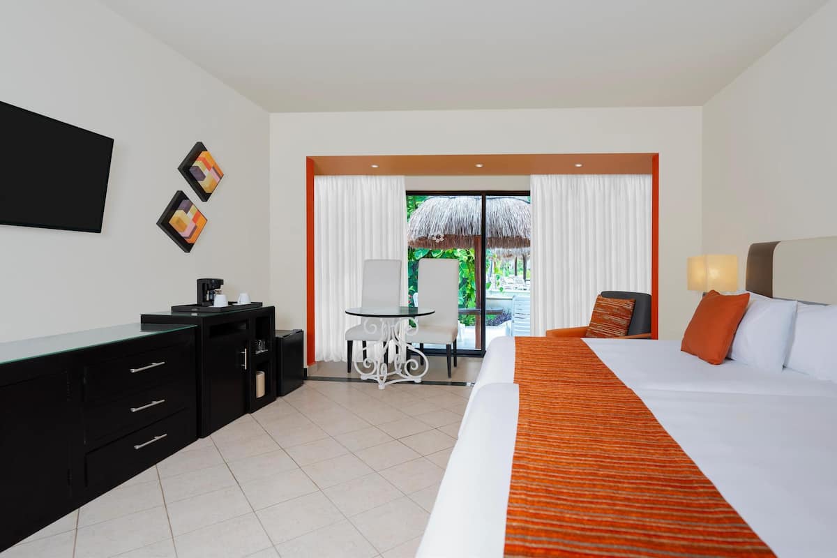 Quarto de hotel com cama, escrivaninha, televisão e vista para o verde lá fora.