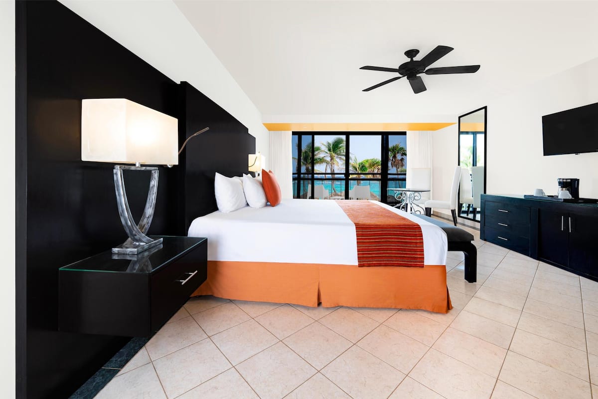 Quarto de hotel moderno com uma cama grande, uma escrivaninha, um ventilador de teto e vista para o mar.