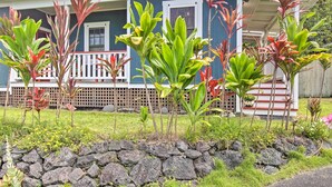 Uma casa com varanda, cercada por plantas tropicais e um muro de pedra.