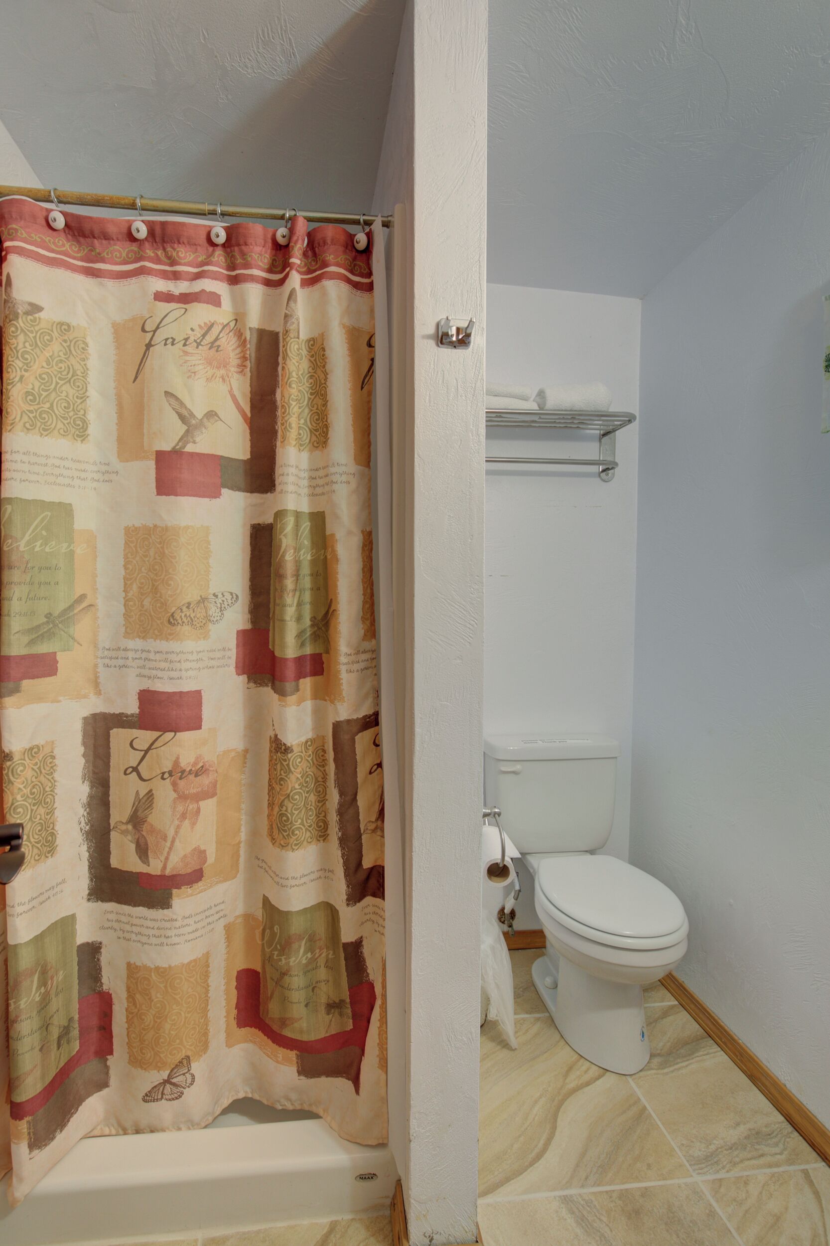 Casa de banho com cortina de chuveiro com texto e padrões estilo vintage, sanita branca e chão em mosaico.