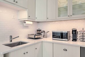 Cozinha moderna com armários brancos, pia de aço inoxidável, micro-ondas e máquina de café.