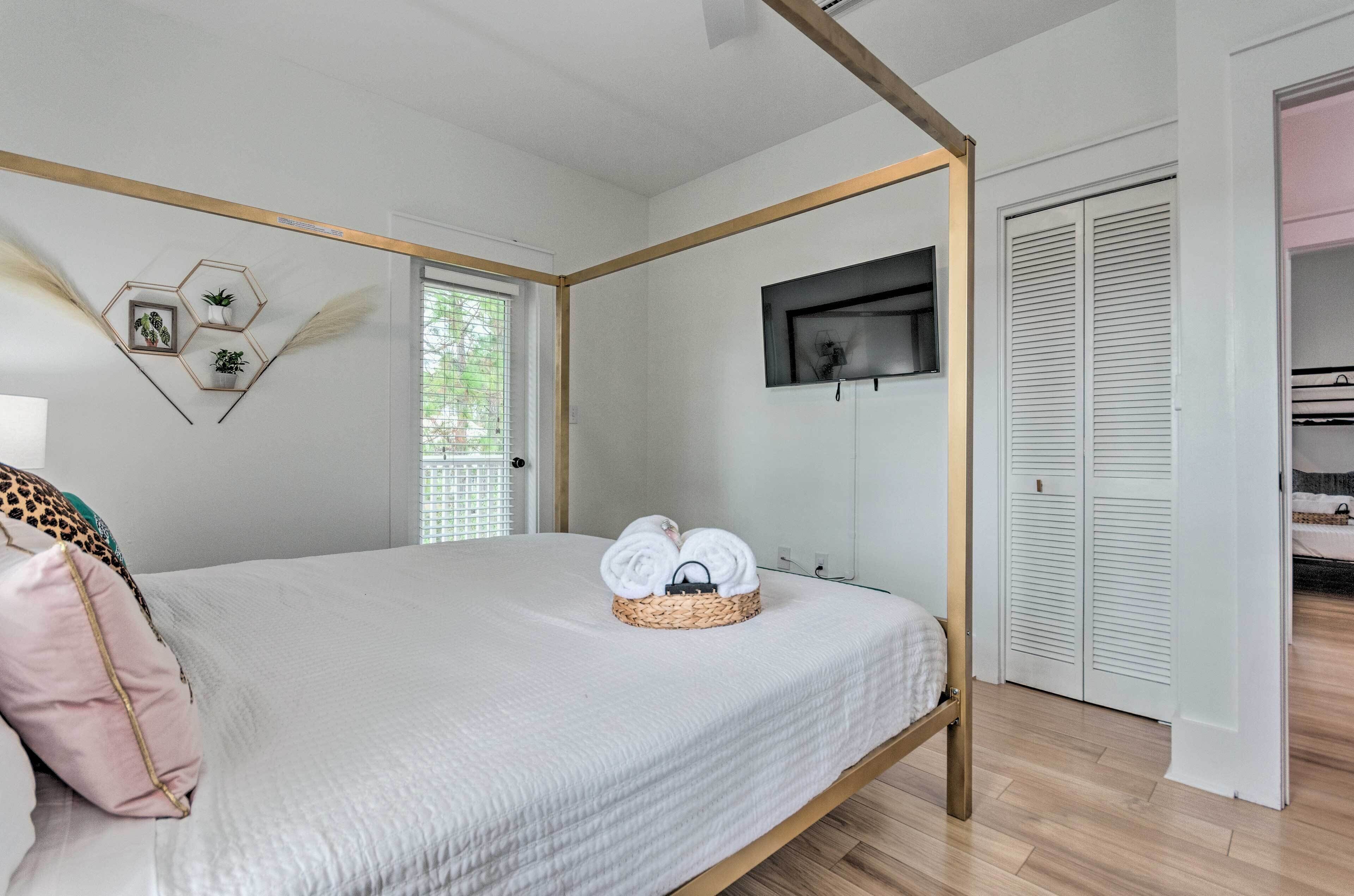 Quarto com cama, guarda-roupa, televisão na parede e janela com persianas.