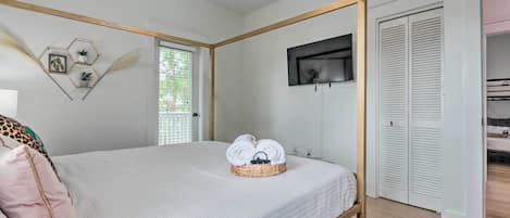 Quarto com cama, guarda-roupa, televisão na parede e janela com persianas.