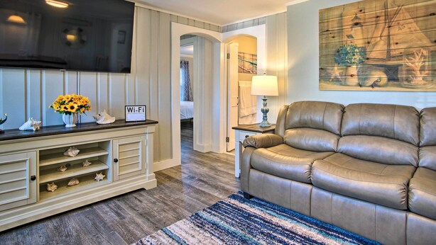 Sala de estar com sofá de couro, televisão, mesa de consola com objetos decorativos e um quadro na parede.