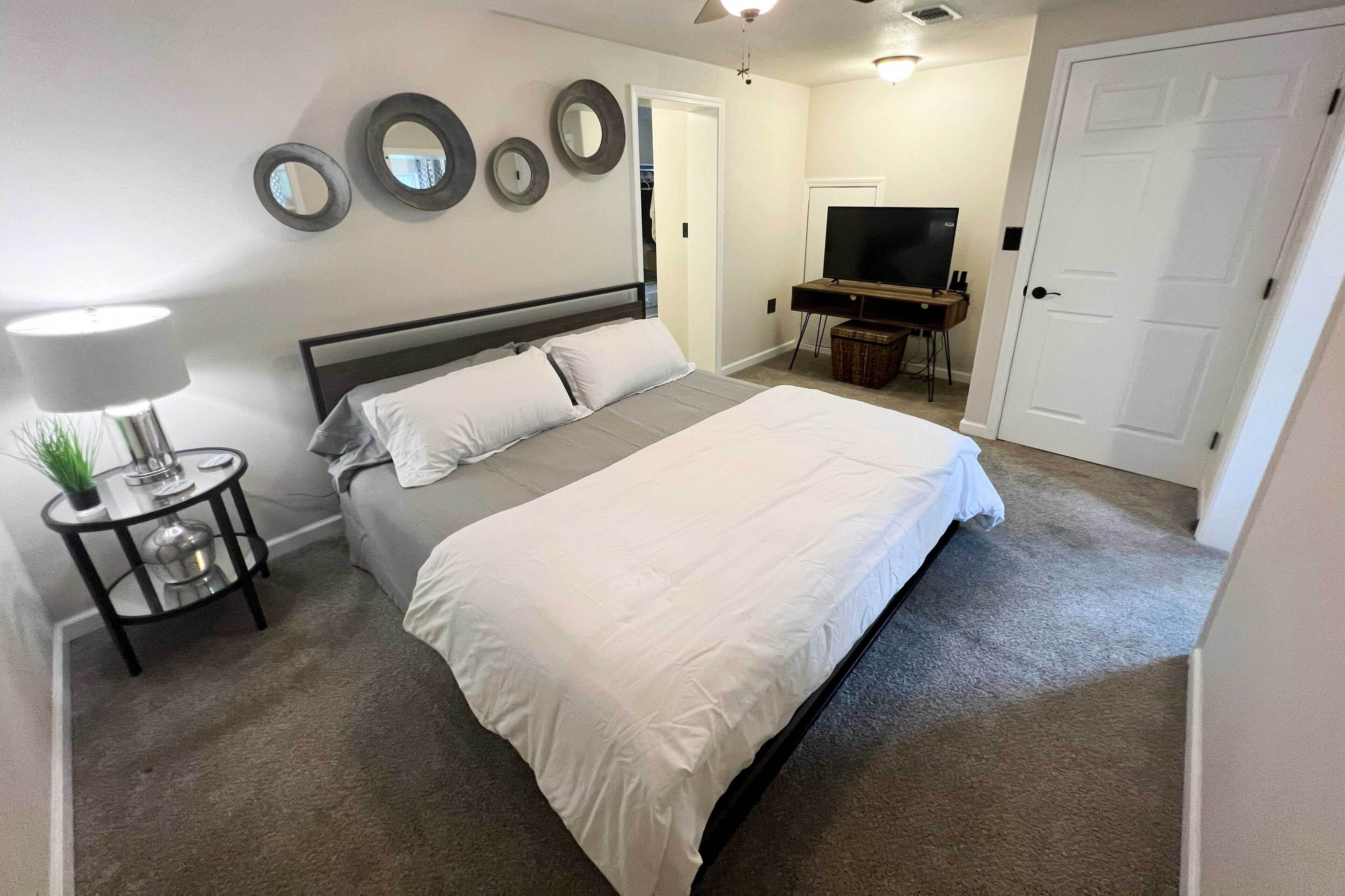 Quarto com cama, escrivaninha e televisão, além de uma porta.