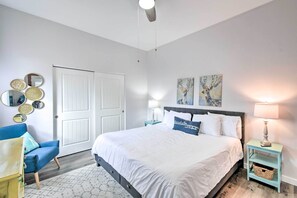 Quarto com cama grande, uma cadeira azul, guarda-roupa branco e uma porta.