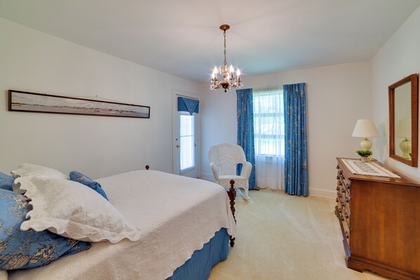 Quarto com cama, cadeira, cômoda, lustre e janela com cortinas.