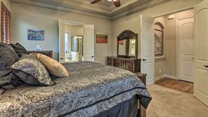 Quarto com cama grande, ventilador de teto, cômoda e porta para outro espaço.