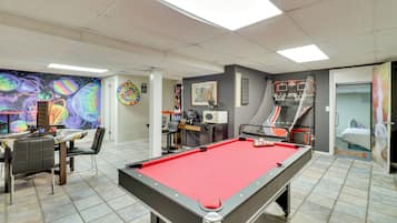 Uma mesa de bilhar numa sala com um mural, um alvo de dardos e um aro de basquete.
