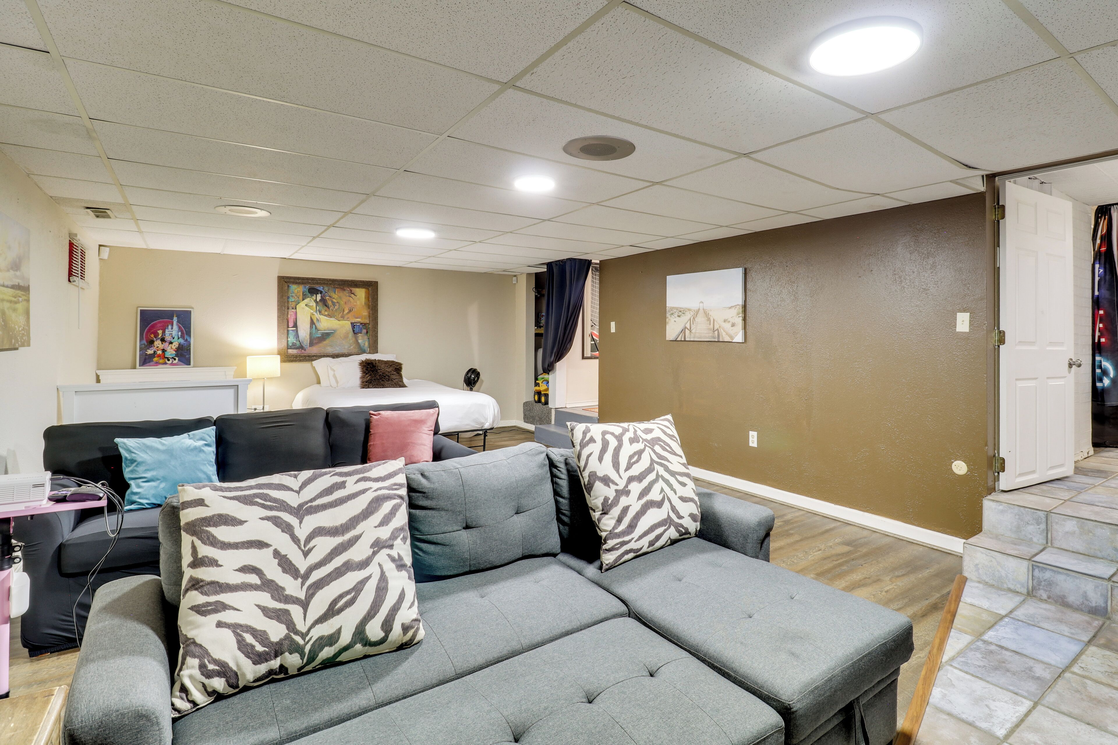 Uma sala de estar com um sofá modular cinza, uma cama, uma escrivaninha e um quadro na parede.