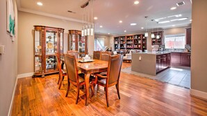 Uma cozinha ampla com piso de madeira, uma sala de jantar com mesa e cadeiras de madeira, e uma área de estar bem iluminada com estantes e um sofá.