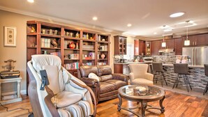 Uma sala de estar espaçosa com poltronas de couro, uma mesa de centro de vidro e uma grande estante repleta de livros e objetos decorativos.
