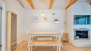 Uma área de refeições com mesa de madeira e bancos, paredes brancas, quadros de peixes emoldurados e uma lareira.
