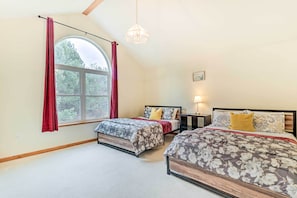Quarto com duas camas, uma janela grande com cortinas vermelhas, um lustre e uma pequena mesa de cabeceira com abajur.