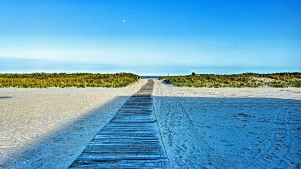 Uma passarela que leva a uma praia com dunas e céu limpo.