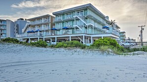 Um hotel à beira-mar com várias varandas, mobiliário de exterior e uma praia de areia em primeiro plano.