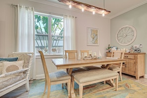 Uma área de refeições com uma mesa de madeira, cadeiras e bancos. Há uma janela com cortinas, um mapa na parede e um relógio.