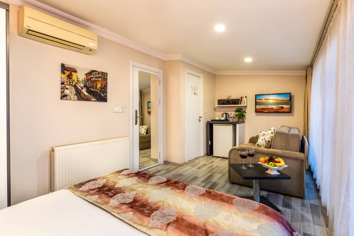 Quarto de hotel com uma cama, um sofá, uma mesinha com frutas e uma televisão.
