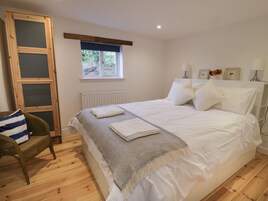 Quarto com uma cama grande, uma cadeira de madeira, uma janela com vista para o verde e um radiador.