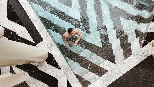 Um homem em uma piscina com design de azulejos geométricos.