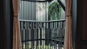 Um corredor com um chão de padrão geométrico, corrimão de metal e vista para o exterior com vegetação.