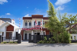 Um edifício de dois andares com uma varanda, um letreiro com a inscrição 'RIYA HOMESTAY' e uma bandeira.