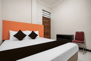 Quarto de hotel com cama, uma cadeira vermelha, televisão e porta de madeira.