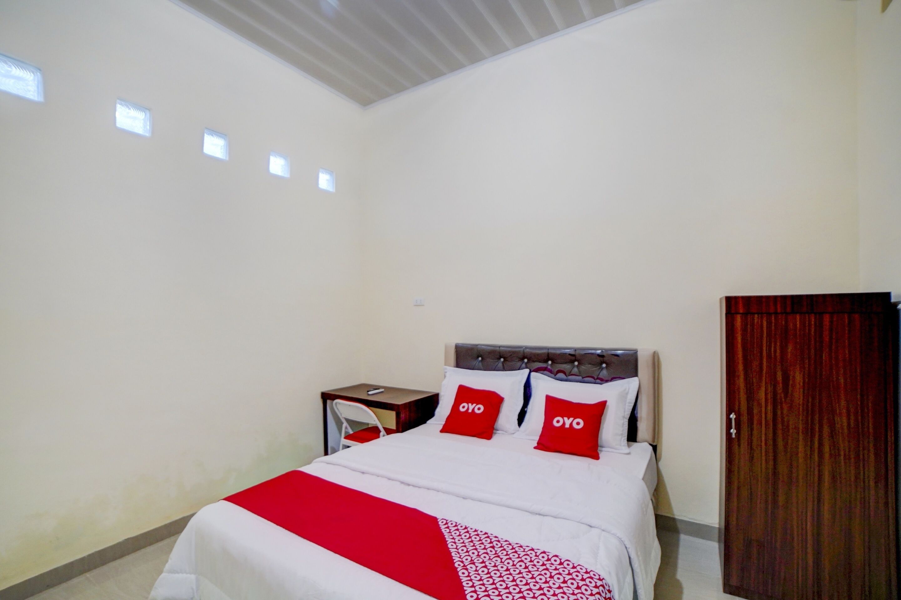 Quarto com cama, duas mesas de cabeceira, um guarda-roupa de madeira e teto com claraboias.