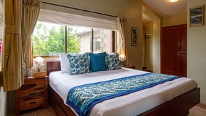 Quarto com uma cama grande, mesa de cabeceira, luminária, janela com cortinas e porta.