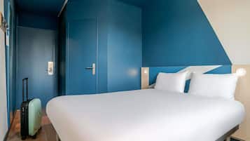 Quarto de hotel com uma cama grande, uma porta, uma mala e um lustre.
