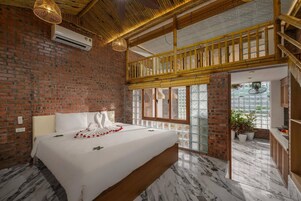 Quarto de hotel com parede de tijolos, cama com roupa de cama branca, teto de madeira e vista através de uma porta de vidro.