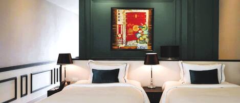 Quarto de hotel com duas camas, um quadro grande na parede e duas luminárias.