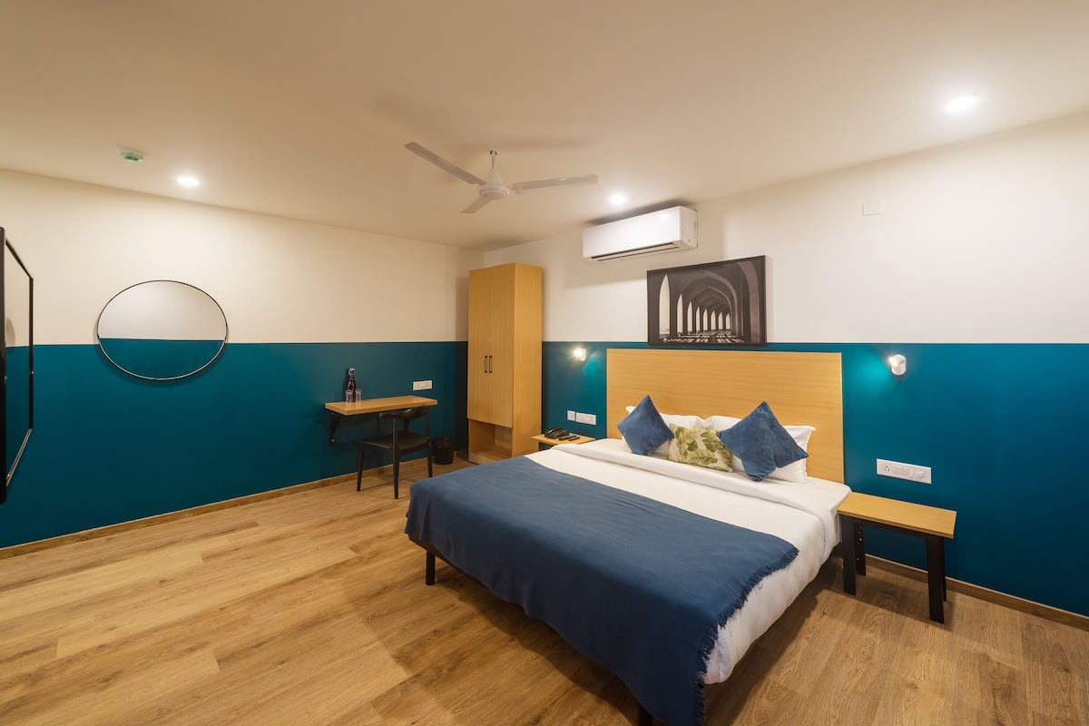 Quarto de hotel com cama, escrivaninha, cadeira, ventilador de teto e aparelho de ar condicionado.