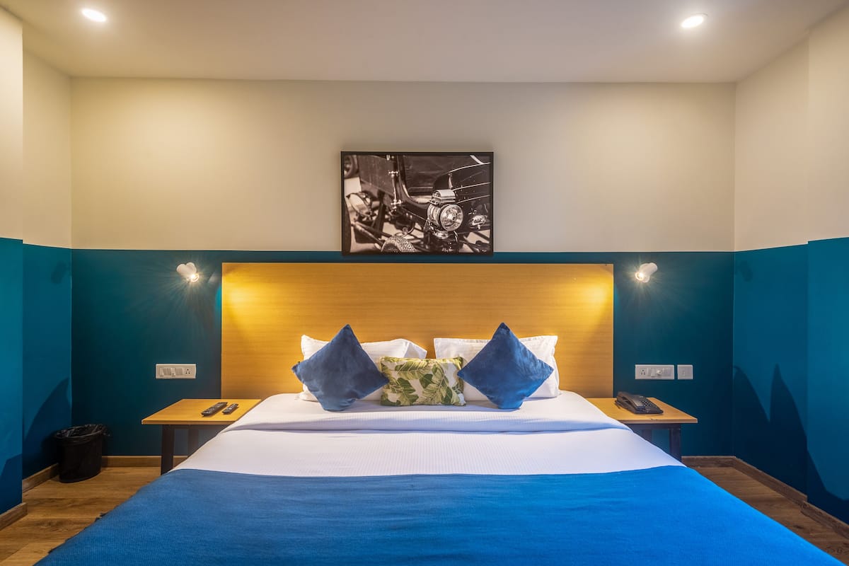 Quarto de hotel com uma cama, mesa de cabeceira, telefone e um quadro pendurado na parede.