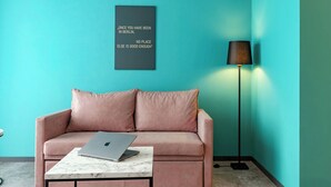 Um quarto com parede verde-água, um sofá rosa, um laptop sobre uma mesa de mármore e um abajur.