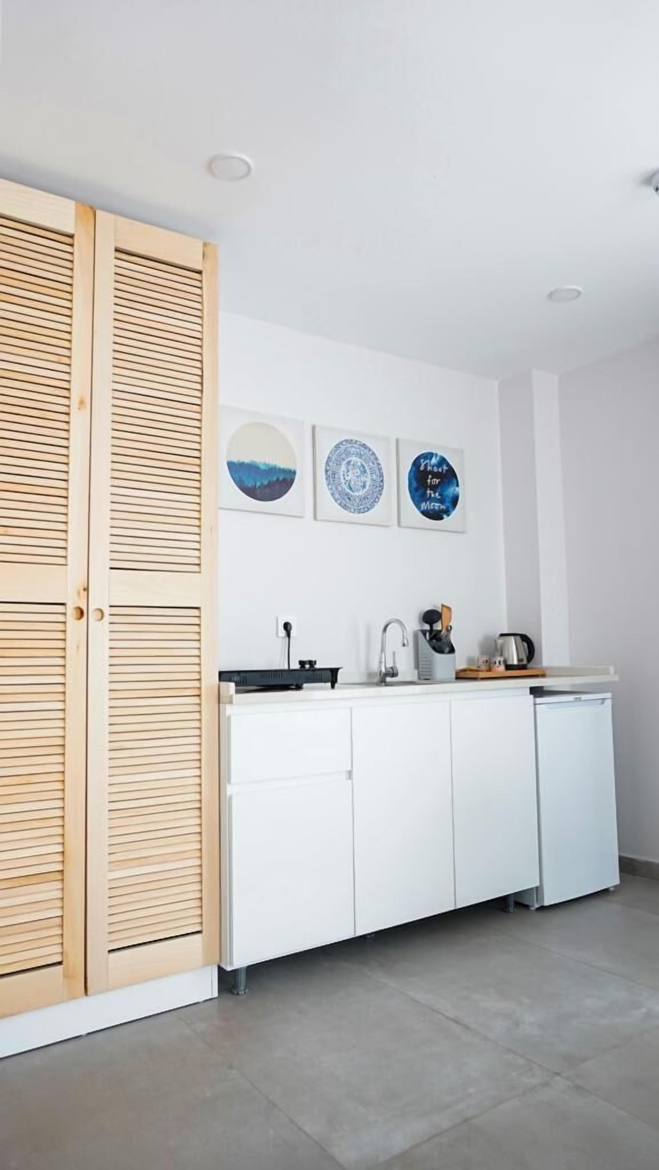 Cozinha moderna com porta de madeira deslizante, armários brancos, pia e três quadros decorativos na parede.