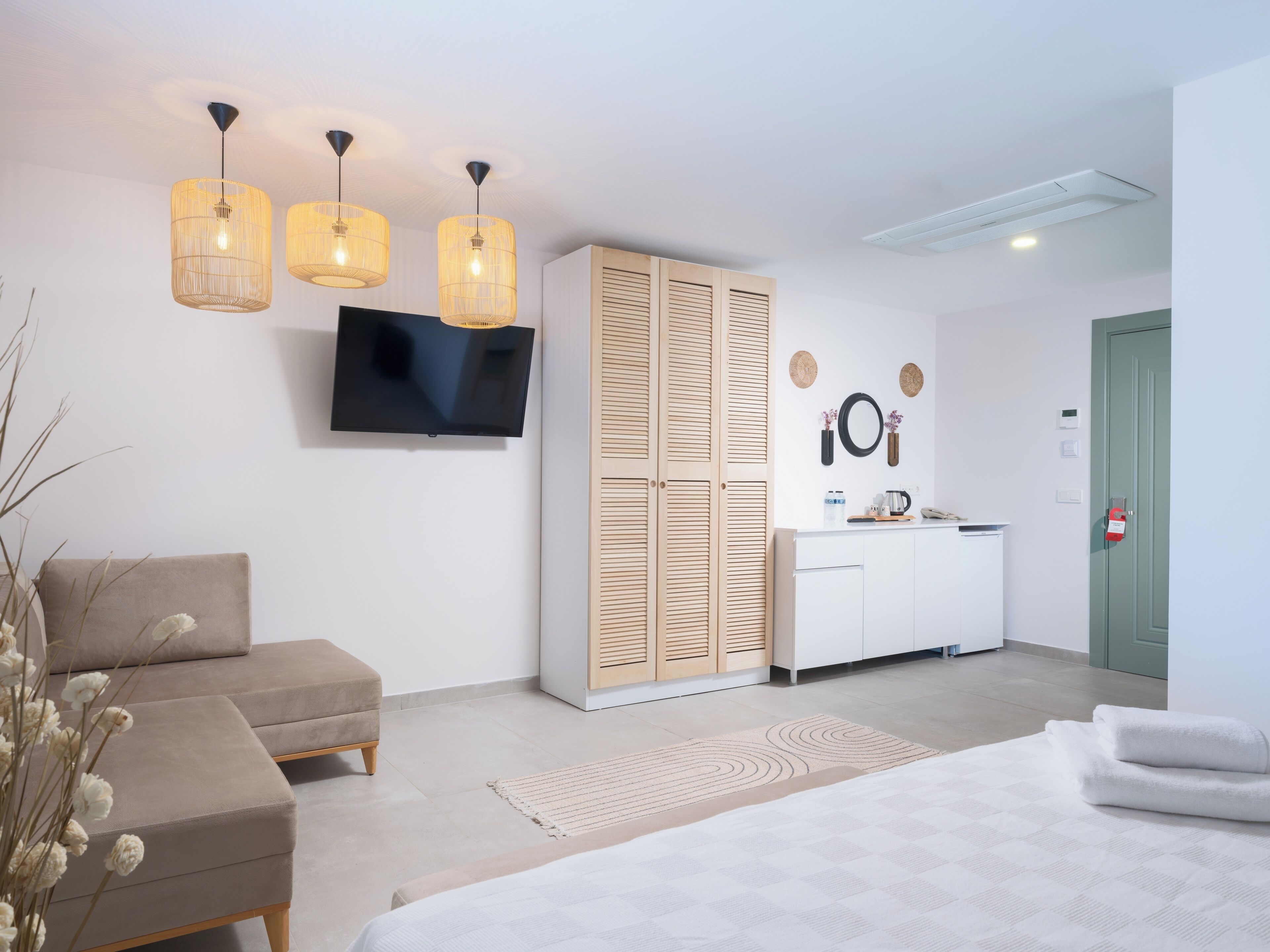 Quarto de hotel moderno com sofá, televisão, guarda-roupa, escrivaninha e cama.
