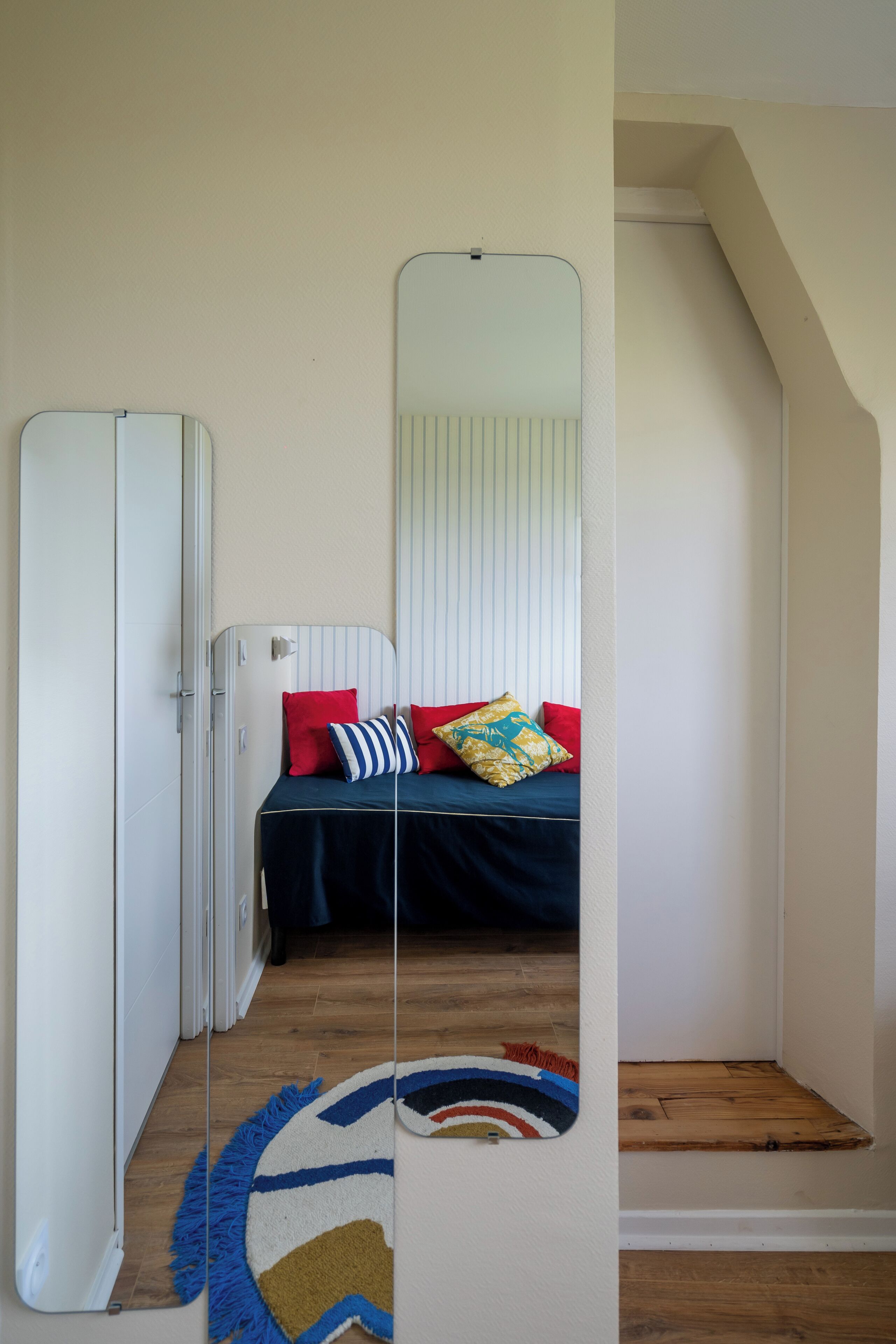 Quarto com cama, espelho, guarda-roupa e um pequeno estrado de madeira.
