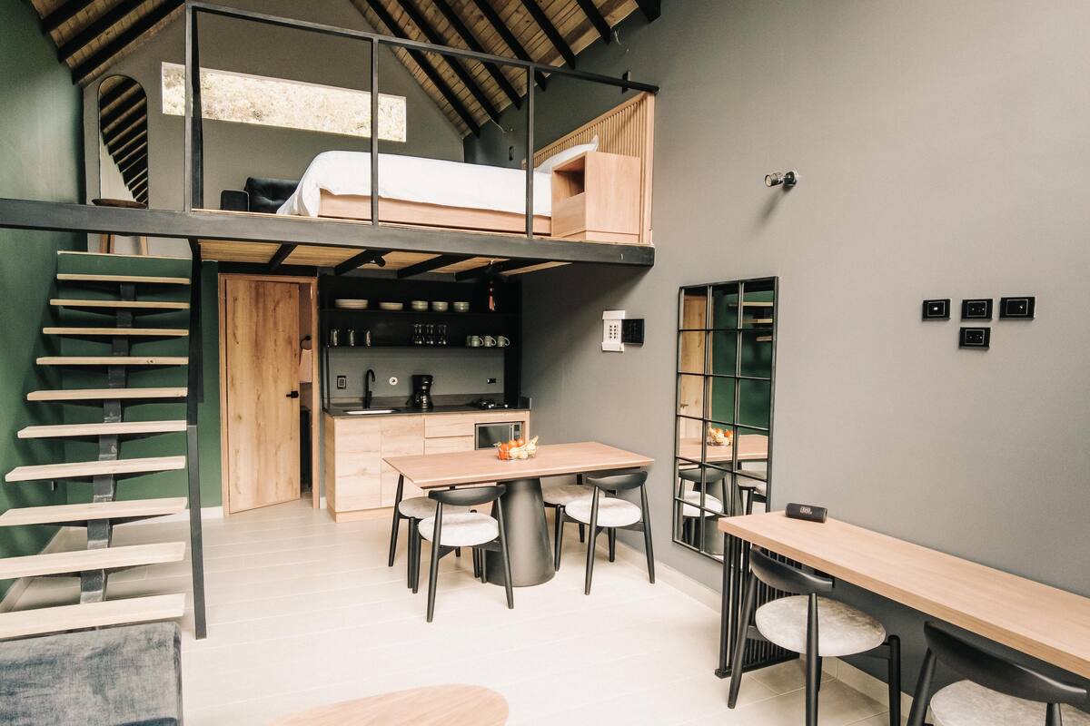 Um apartamento compacto e moderno com um quarto em mezzanine, uma cozinheneta e um espaço de jantar.
