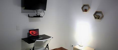 Um quarto pequeno com uma escrivaninha, uma cadeira, uma televisão na parede e duas decorações hexagonais.